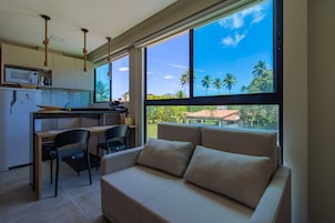 Cozinha moderna com área de jantar, grandes janelas com vista para palmeiras e um sofá em primeiro plano.