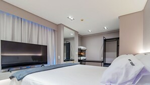 Quarto de hotel com uma cama grande, televisão de tela plana, espelho, mesa de cabeceira e guarda-roupa.