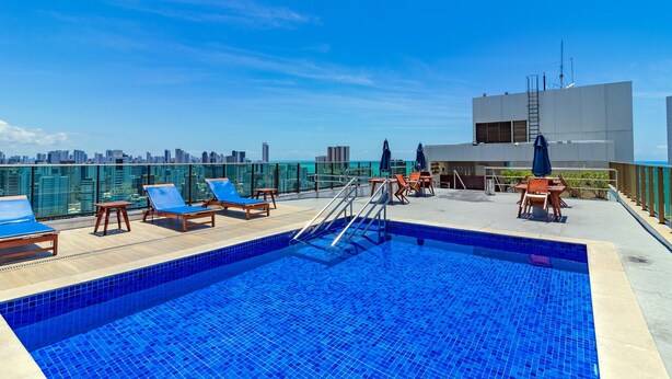 Piscina no terraço com azulejos azuis, espreguiçadeiras e vista para o horizonte da cidade.