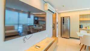 Uma cozinha moderna com frigorífico embutido, uma grande televisão de ecrã plano na parede e uma área de refeições com uma mesa e cadeiras brancas.