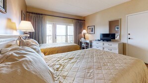 Quarto de hotel com duas camas, uma escrivaninha com cadeira, televisão e guarda-roupa.