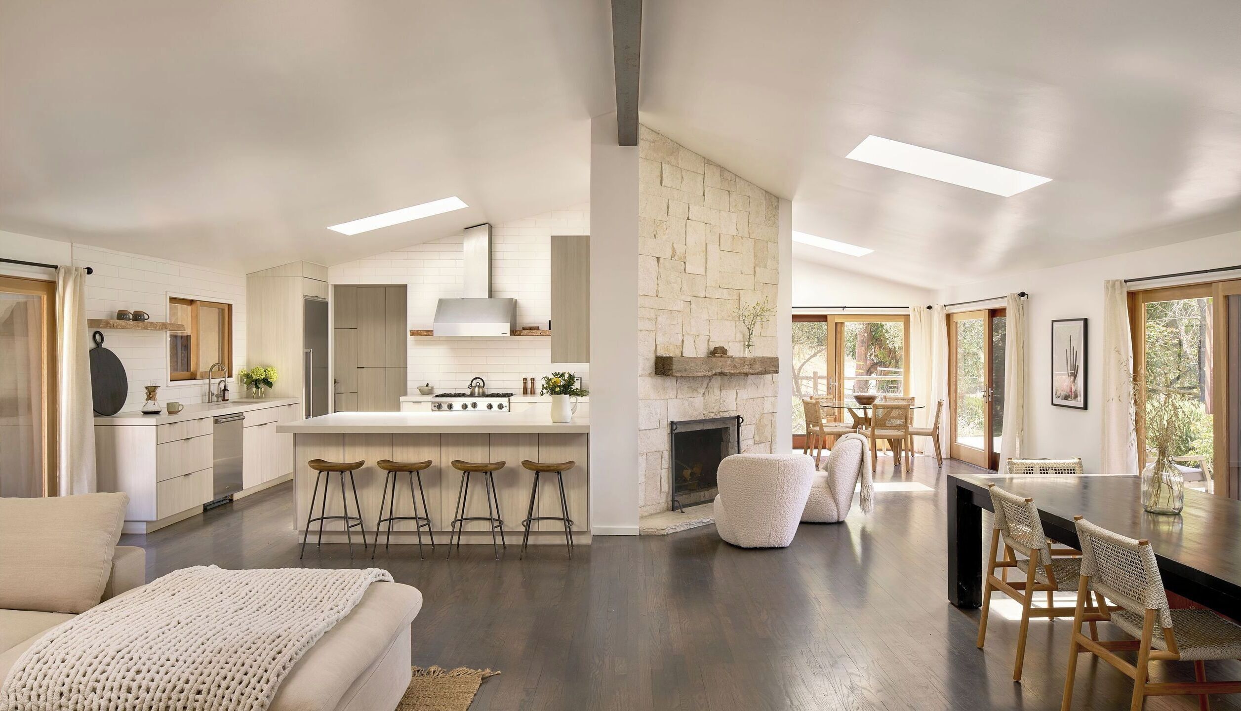 Uma cozinha moderna com ilha central, banquetas, lareira e área de jantar com luz natural.
