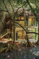 Uma casa moderna com fachada de vidro, rodeada por árvores e um lago.