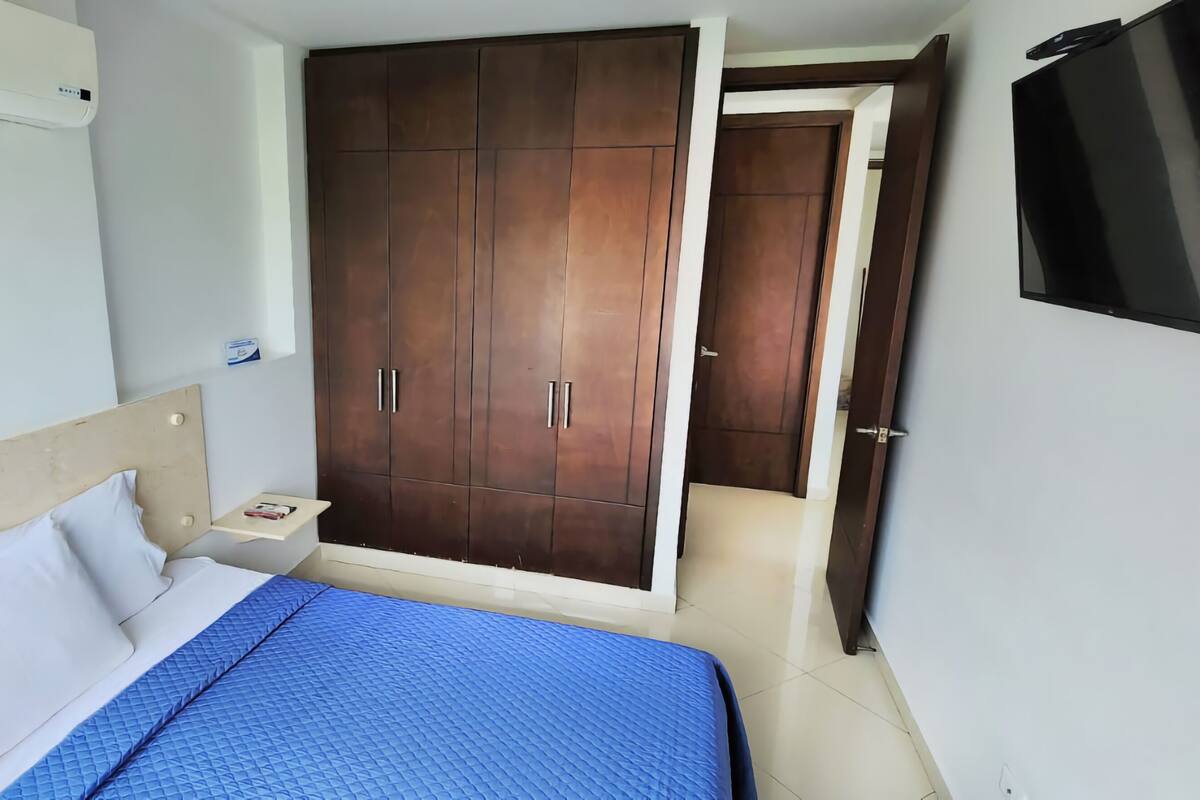 Quarto com cama, guarda-roupa, televisão e uma pequena mesa de cabeceira.