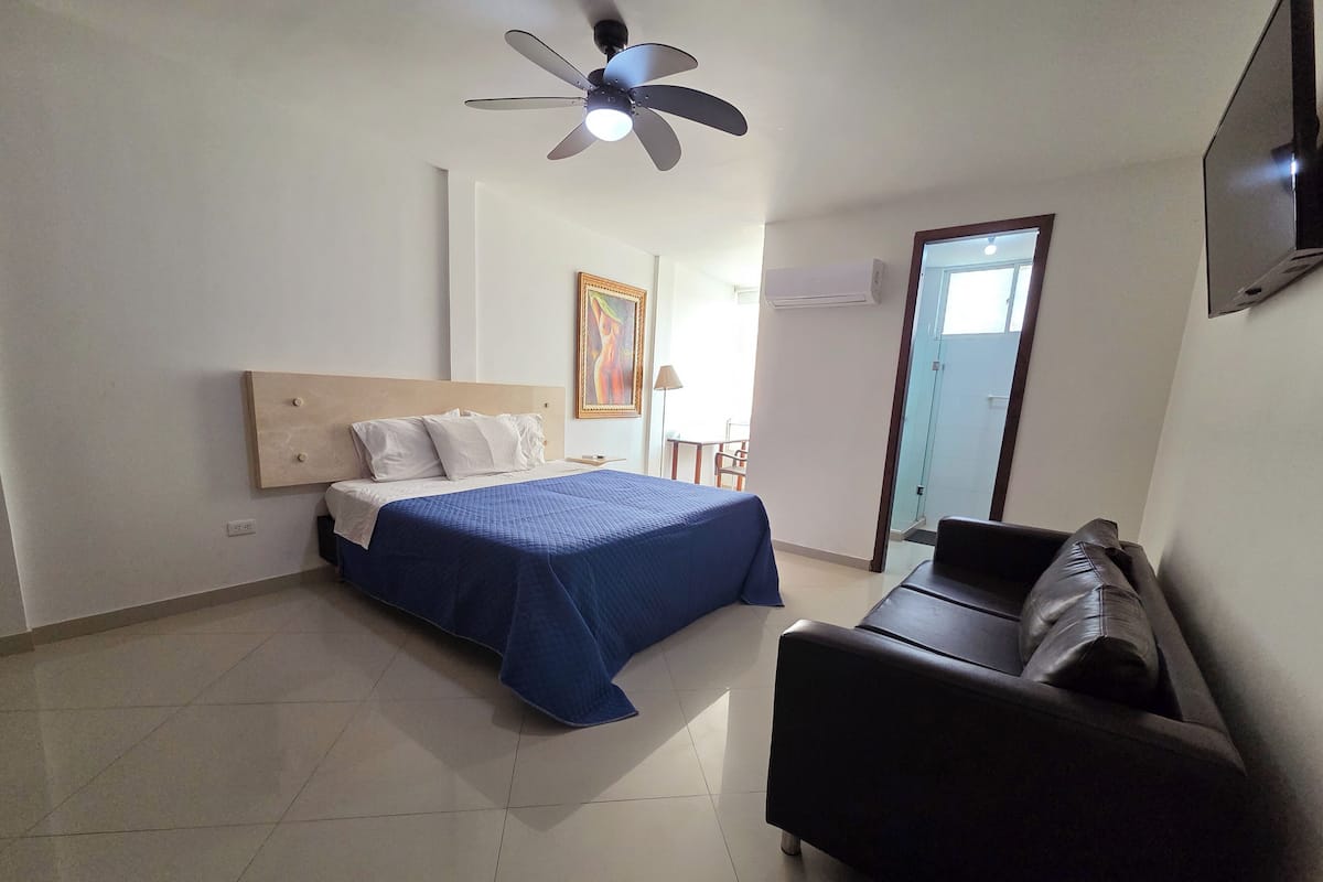 Quarto com cama, ventilador de teto, televisão e porta que dá para uma varanda.