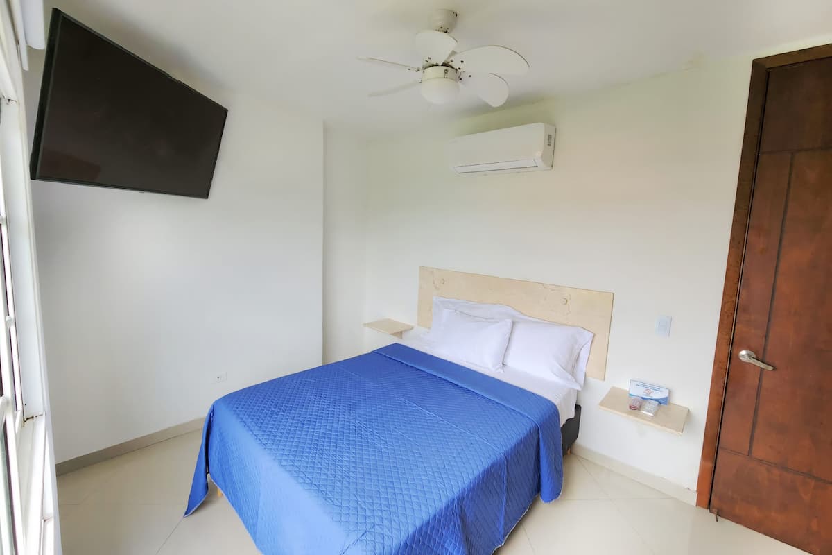 Quarto com cama, ventilador de teto, ar-condicionado, televisão e porta de madeira.