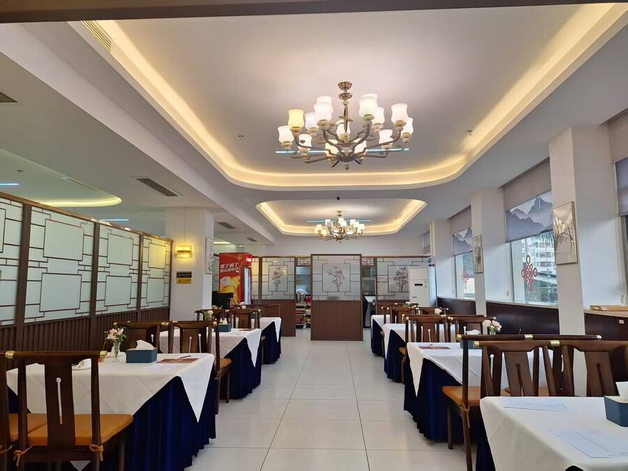 Um restaurante com disposição de mesas alongada, um candelabro e obras de arte emolduradas nas paredes.