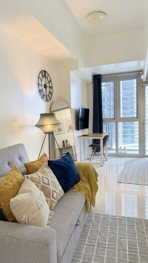 Uma sala de estar moderna com sofá, luminária, TV de tela plana e uma grande janela com vista para a cidade.