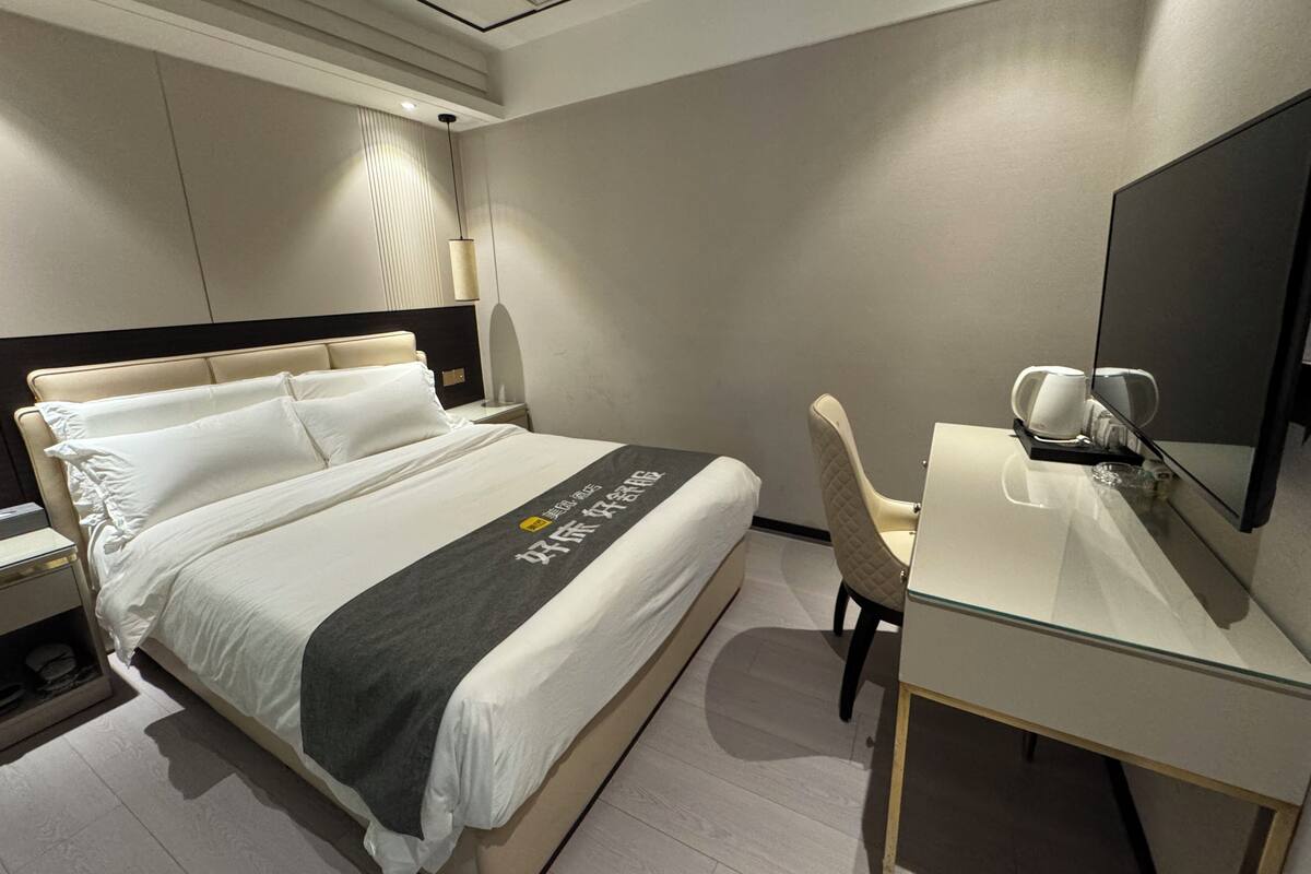 Quarto de hotel com cama, escrivaninha, cadeira, televisão de tela plana e mesa de cabeceira com abajur.