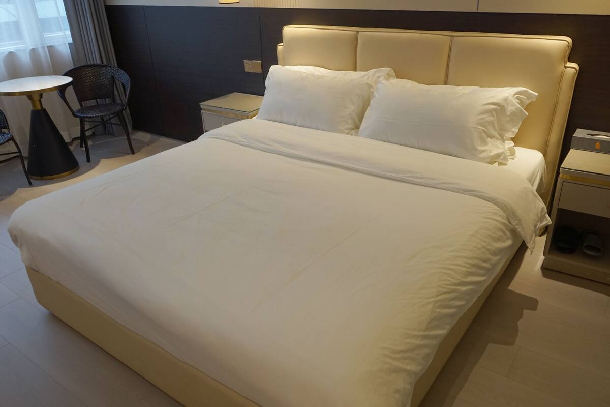 Quarto de hotel com uma cama grande, mesa de cabeceira, uma cadeira e uma pequena mesa.