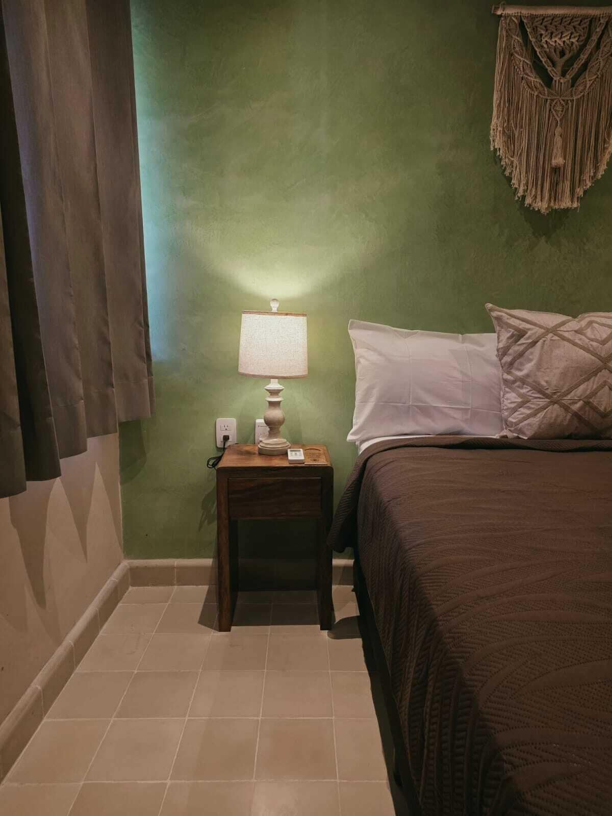Quarto com uma cama, uma mesa de cabeceira com abajur e um objeto pendurado na parede.