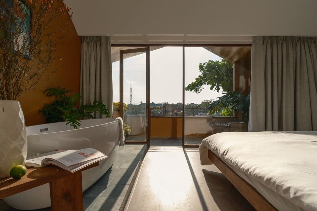 Quarto de hotel com cama, sofá, banheira e uma ampla janela com vista para a cidade.