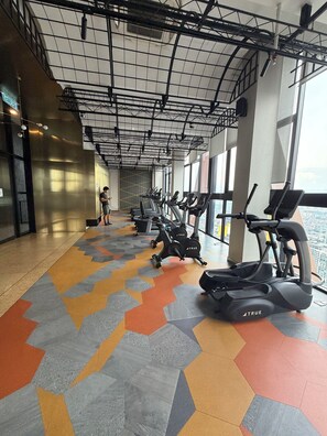 Uma academia com equipamentos de exercícios, piso estampado e janelas amplas.