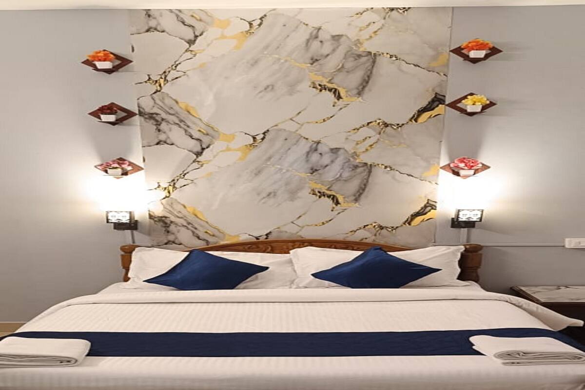 Cama bem arrumada com uma parede de padrão marmorizado ao fundo, duas luminárias de apoio e uma cabeceira de madeira.