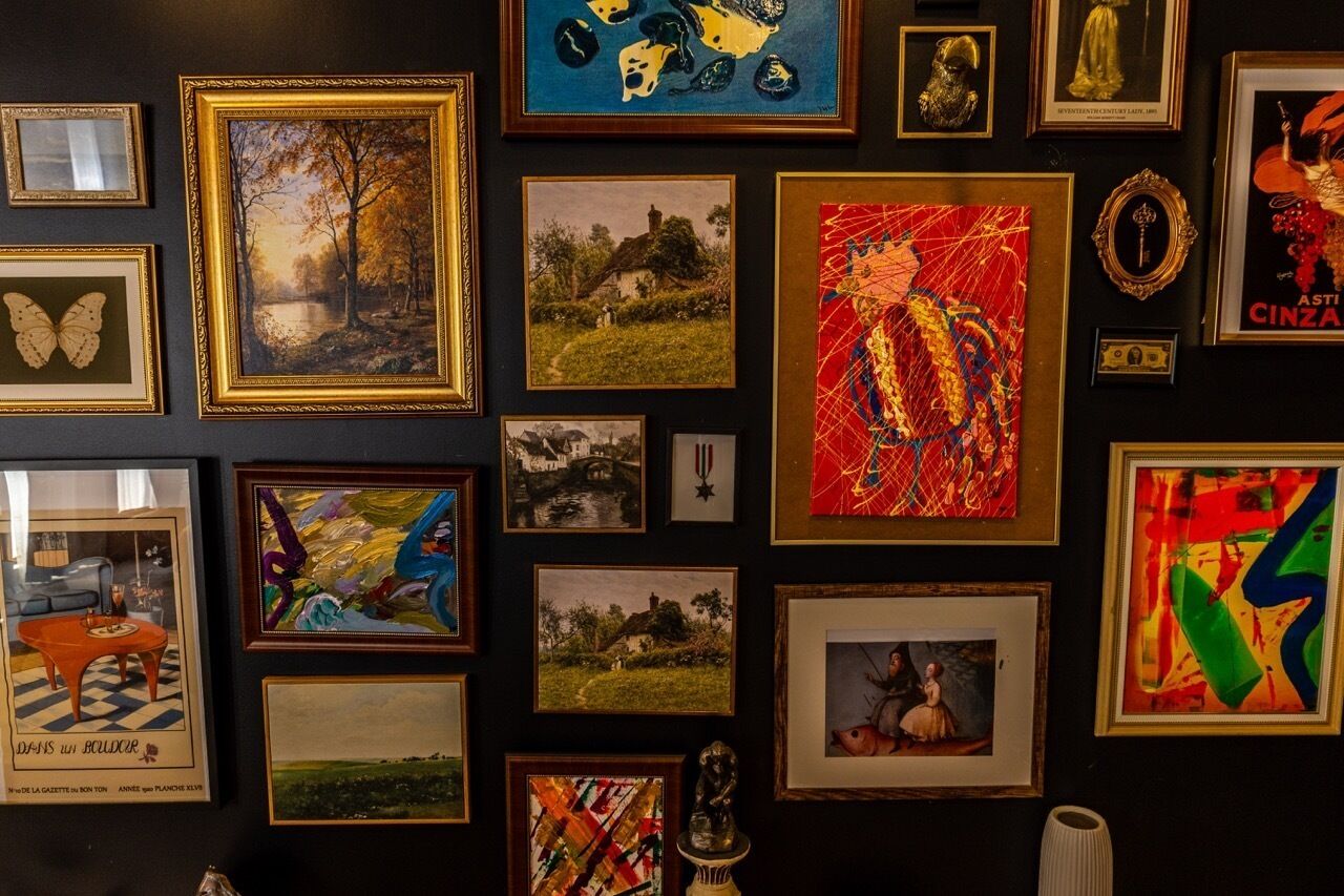 Uma parede com diversas obras de arte emolduradas, incluindo pinturas e gravuras.