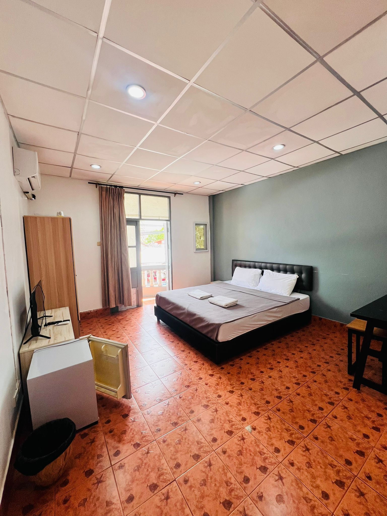Quarto de hotel com cama, escrivaninha, cadeira, guarda-roupa e janela.