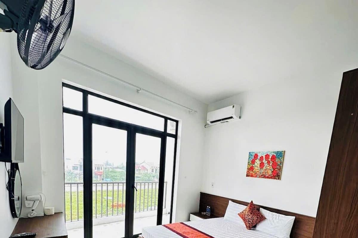 Quarto com cama grande, ventilador de teto, televisão e varanda com vista.