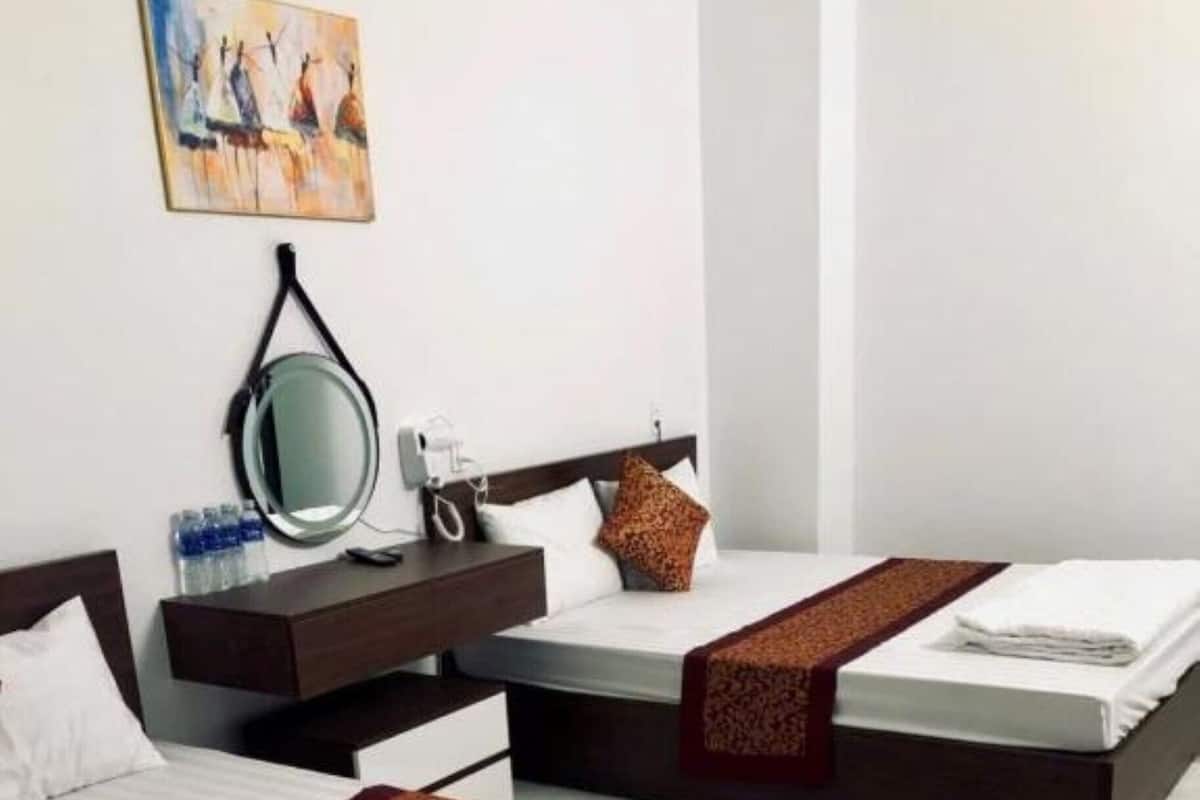 Quarto de hotel com duas camas, uma mesinha de cabeceira com espelho, uma escrivaninha pequena e um quadro na parede.