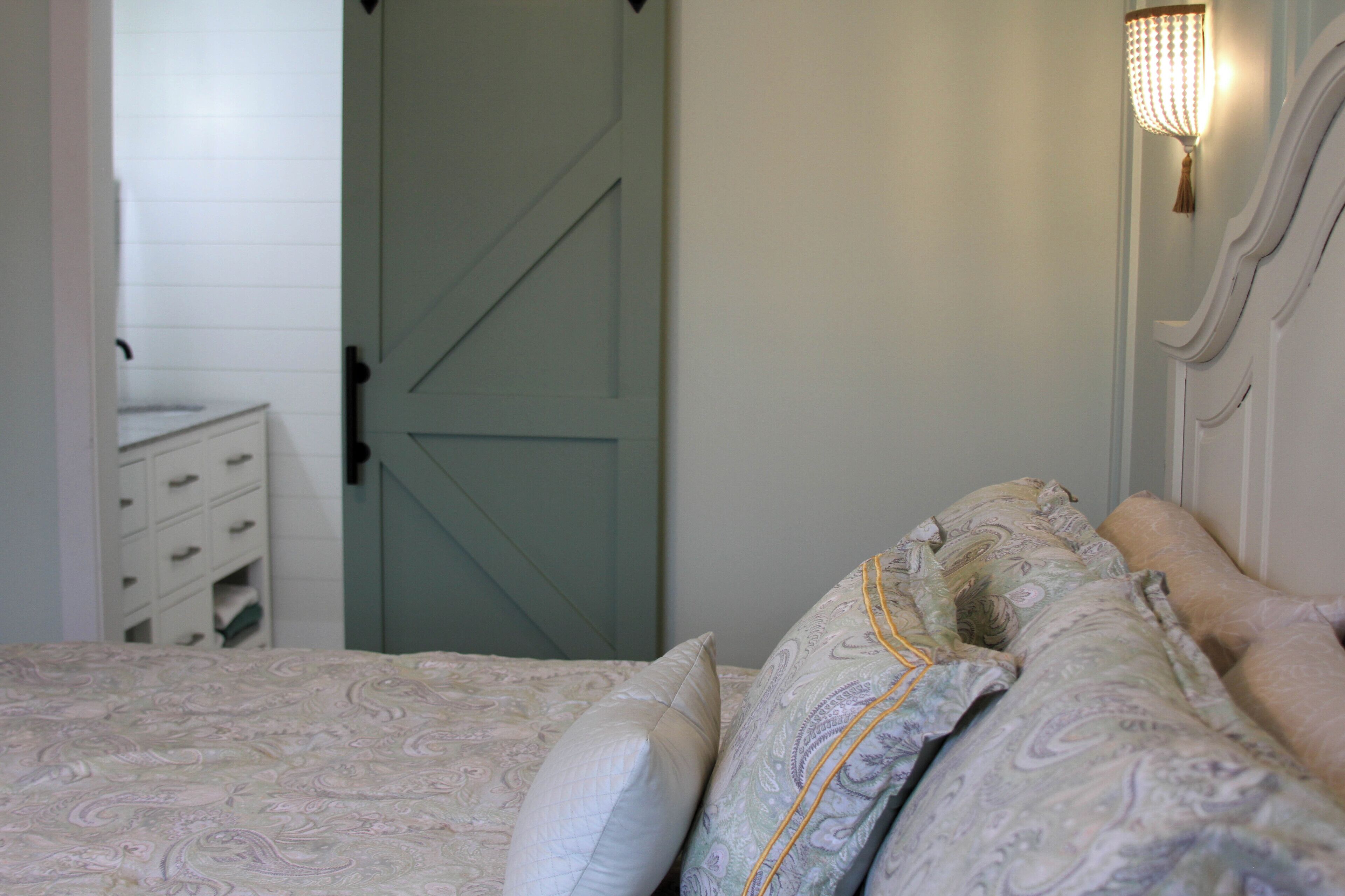 Quarto com cama, roupa de cama estampada, penteadeira e porta.