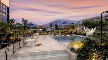 Uma área de piscina no terraço, com escadas que descem, cercada por vegetação e paisagem urbana ao fundo.