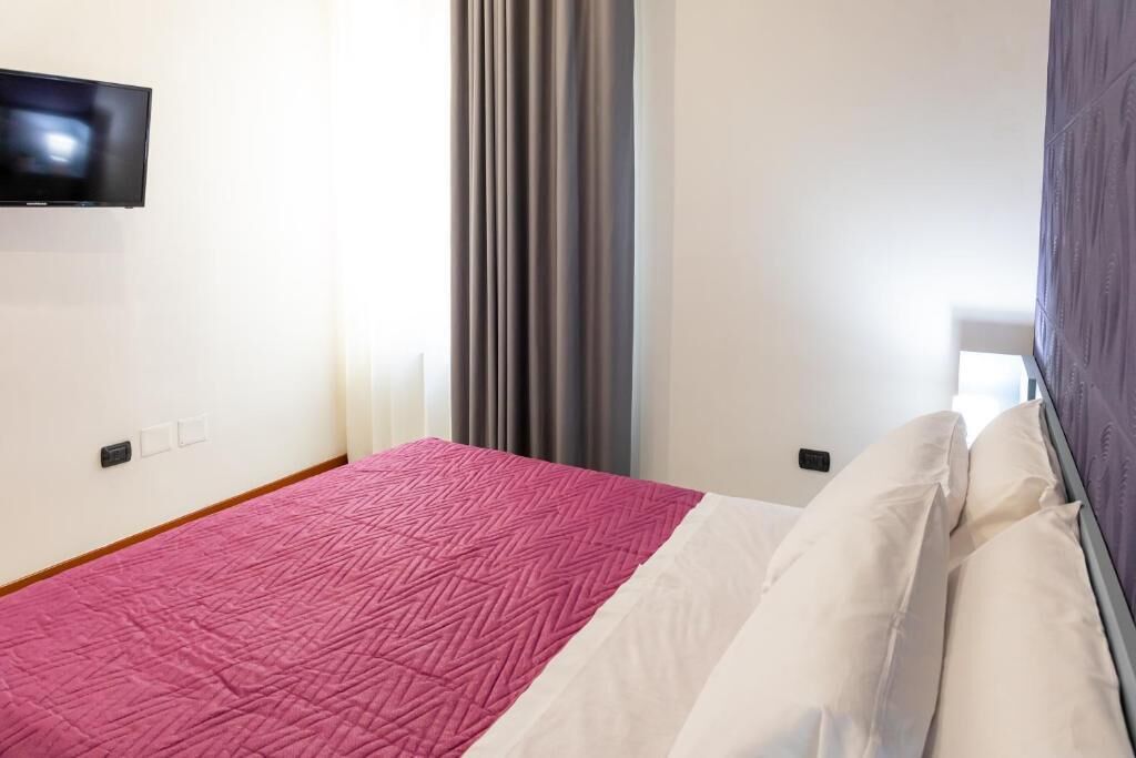 Quarto de hotel com uma cama, televisão na parede e janela com cortinas.