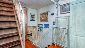 Uma escadaria de madeira com corrimão de corda, um quadro de uma paisagem costeira e uma porta com detalhes em forma de concha.