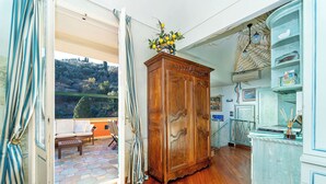 Quarto com armário de madeira, uma mesinha e vista para uma encosta através de uma porta aberta.