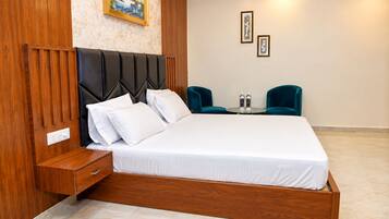 Quarto de hotel com estrutura de cama de madeira, mesa de cabeceira e duas cadeiras verde-água.