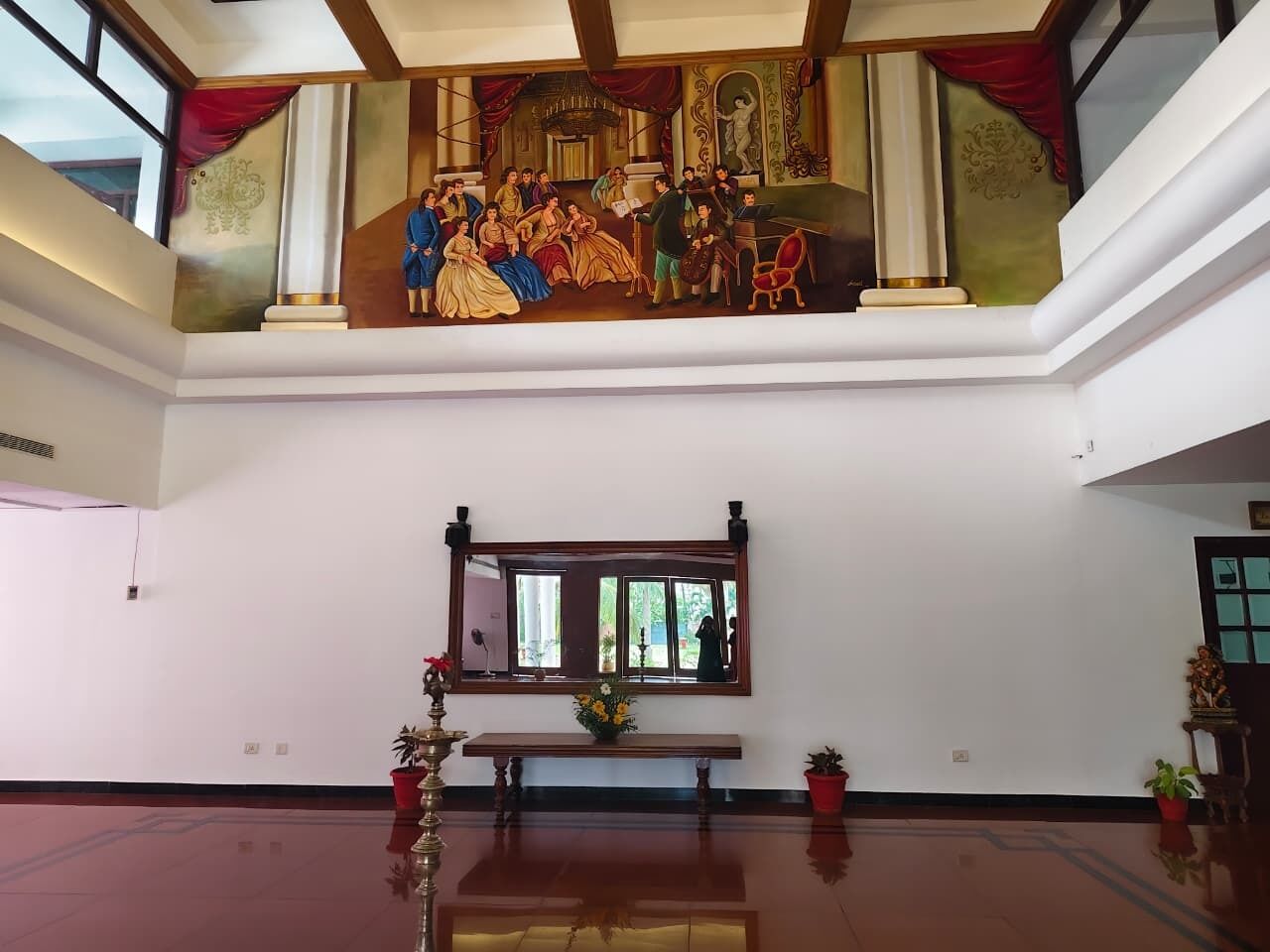 Um salão amplo com teto alto, um espelho grande e um mural retratando uma cena histórica.
