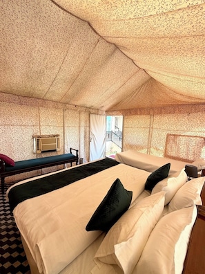 Um quarto tipo tenda com duas camas, um banco, uma janela com cortinas e um ar condicionado fixado na parede.