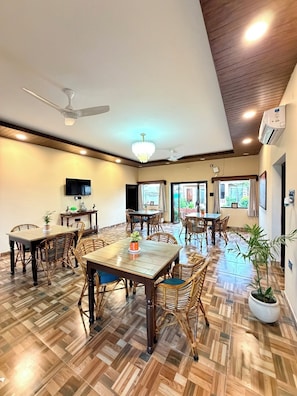 Uma sala de jantar com piso de madeira, móveis de vime, ventiladores de teto e um candelabro.