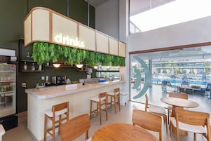 Uma área de bar moderna com um letreiro 'drinks', banquetas de madeira e vista para a piscina.