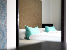 Quarto de hotel com uma cama, duas almofadas, cabeceira e parede texturizada.