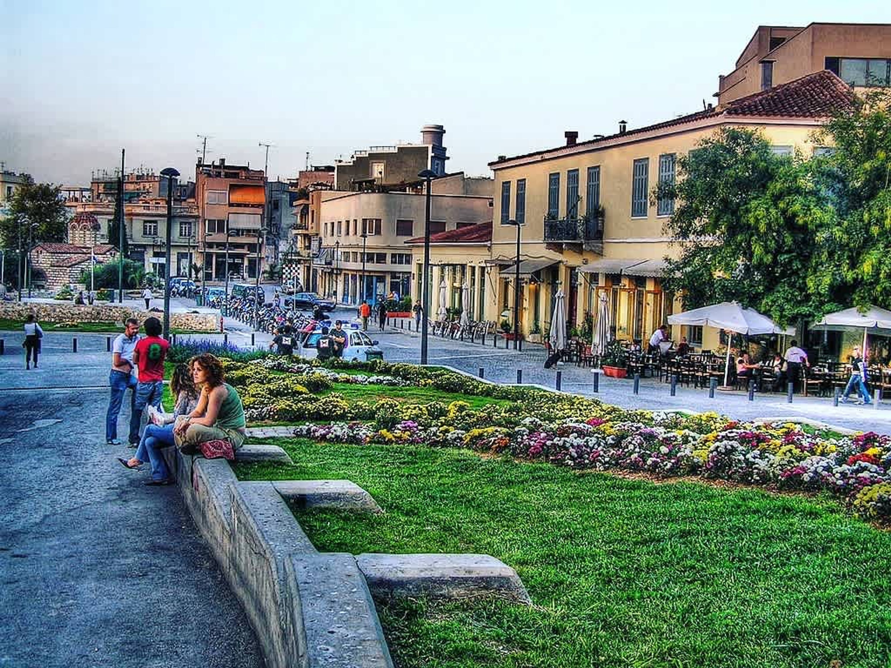 Uma praça pública com bancos, um jardim de flores e edifícios ao fundo.