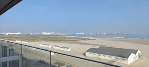 Vista de uma varanda com vista para uma praia, com alguns edifícios, incluindo uma construção branca com telhado escuro.