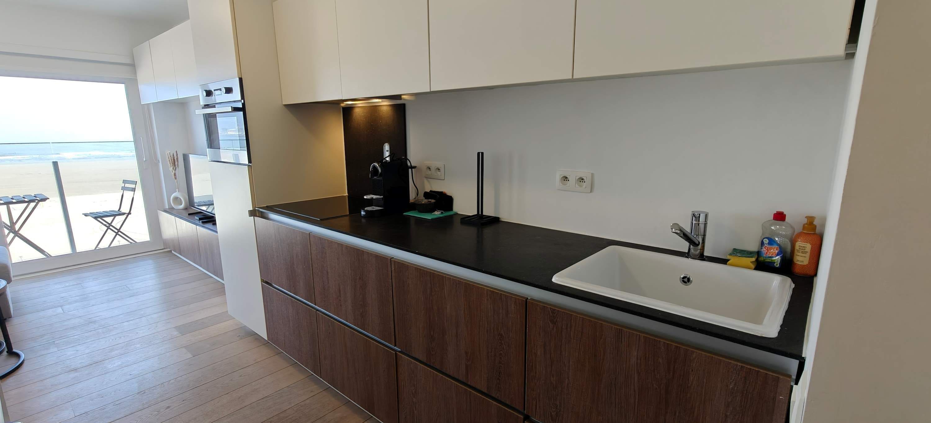 Cozinha moderna com bancada preta, armários de madeira e vista para a praia.
