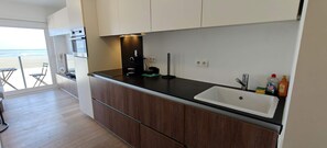 Cozinha moderna com bancada preta, armários de madeira e vista para a praia.