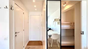 Quarto moderno e minimalista com piso de madeira, paredes brancas e uma porta branca, além de um espelho grande.