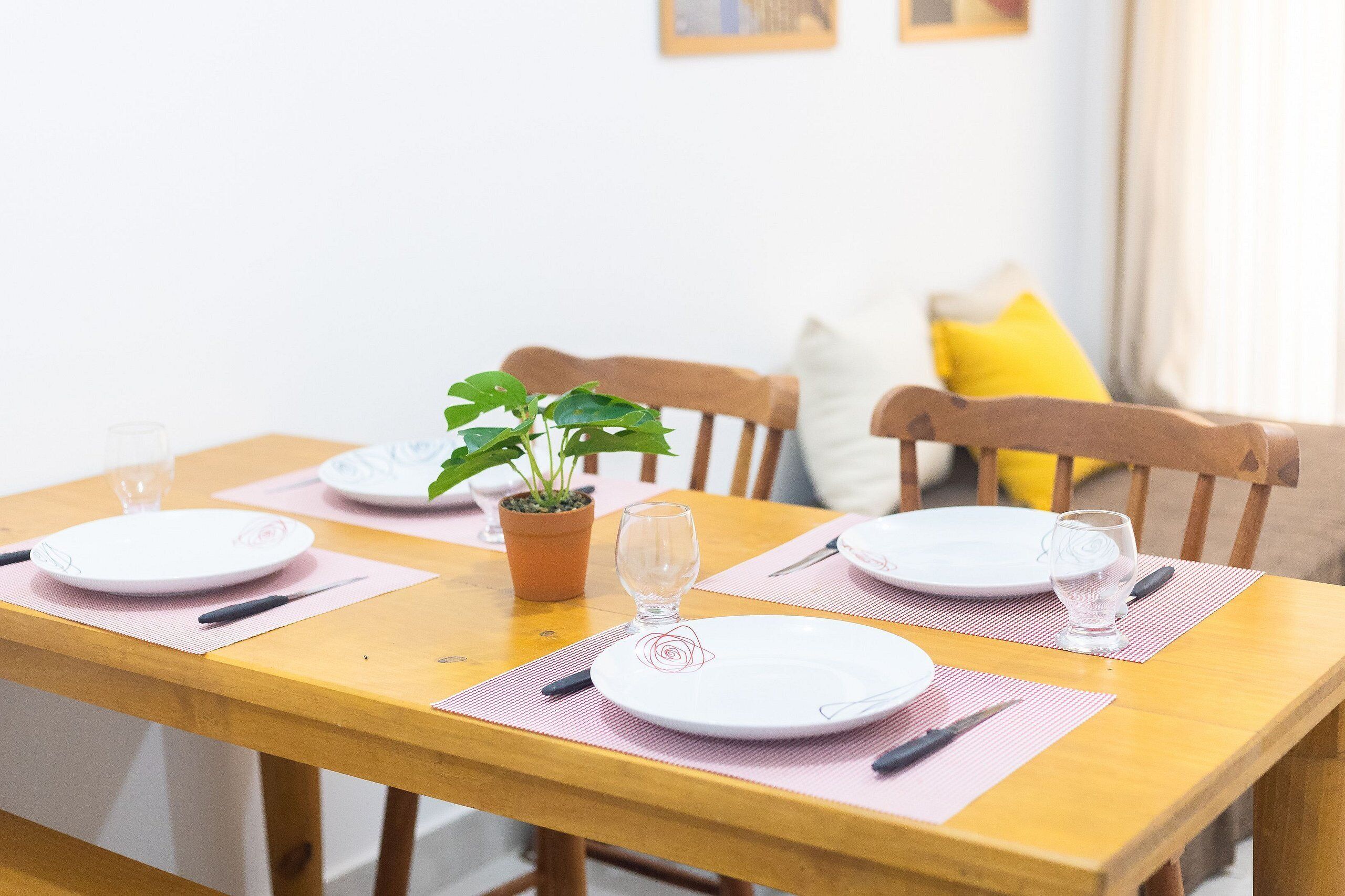 Uma mesa de jantar posta com pratos, talheres e um vaso de planta.