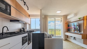 Cozinha moderna com bancada preta, armários brancos e forno embutido. Há uma janela grande com vista para o exterior.