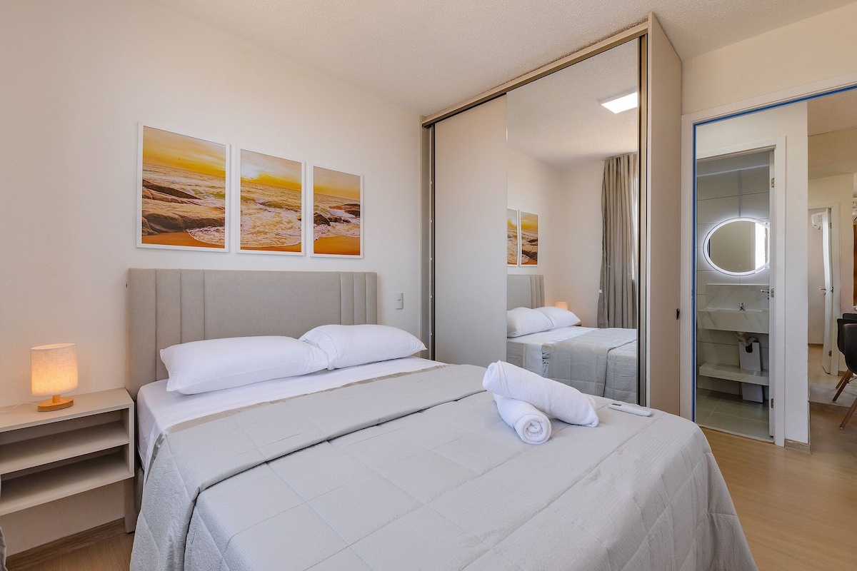 Quarto de hotel com cama, mesa de cabeceira, espelho e obras de arte na parede.