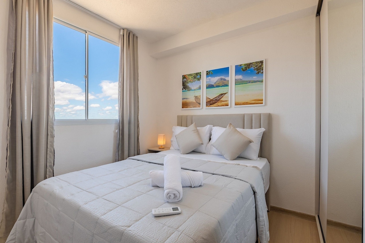 Quarto de hotel com cama, controle remoto e janela com cortinas.