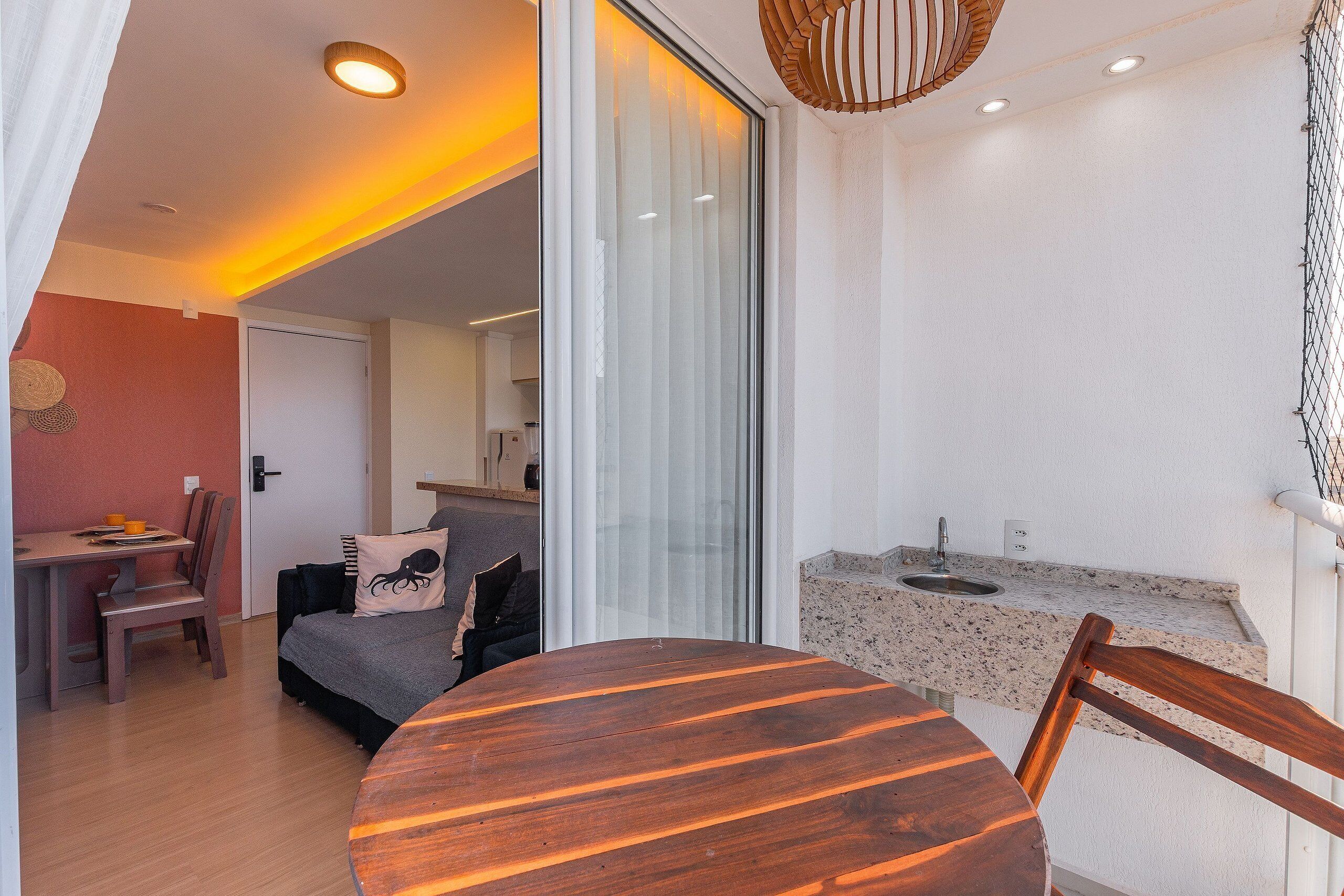 Uma sala de estar moderna com uma mesa de jantar de madeira, um sofá e uma área de cozinha com pia e bancada.