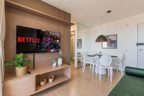 Uma sala de estar moderna com televisão de tela plana, uma área de jantar com cadeiras brancas e um sofá verde.