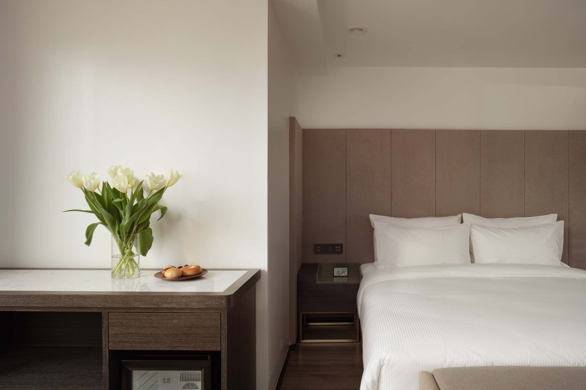 Quarto de hotel com cama, mesa de cabeceira e um vaso de flores.
