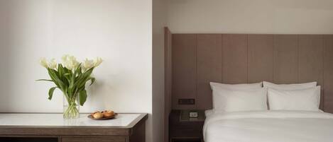 Quarto de hotel com cama, mesa de cabeceira e um vaso de flores.