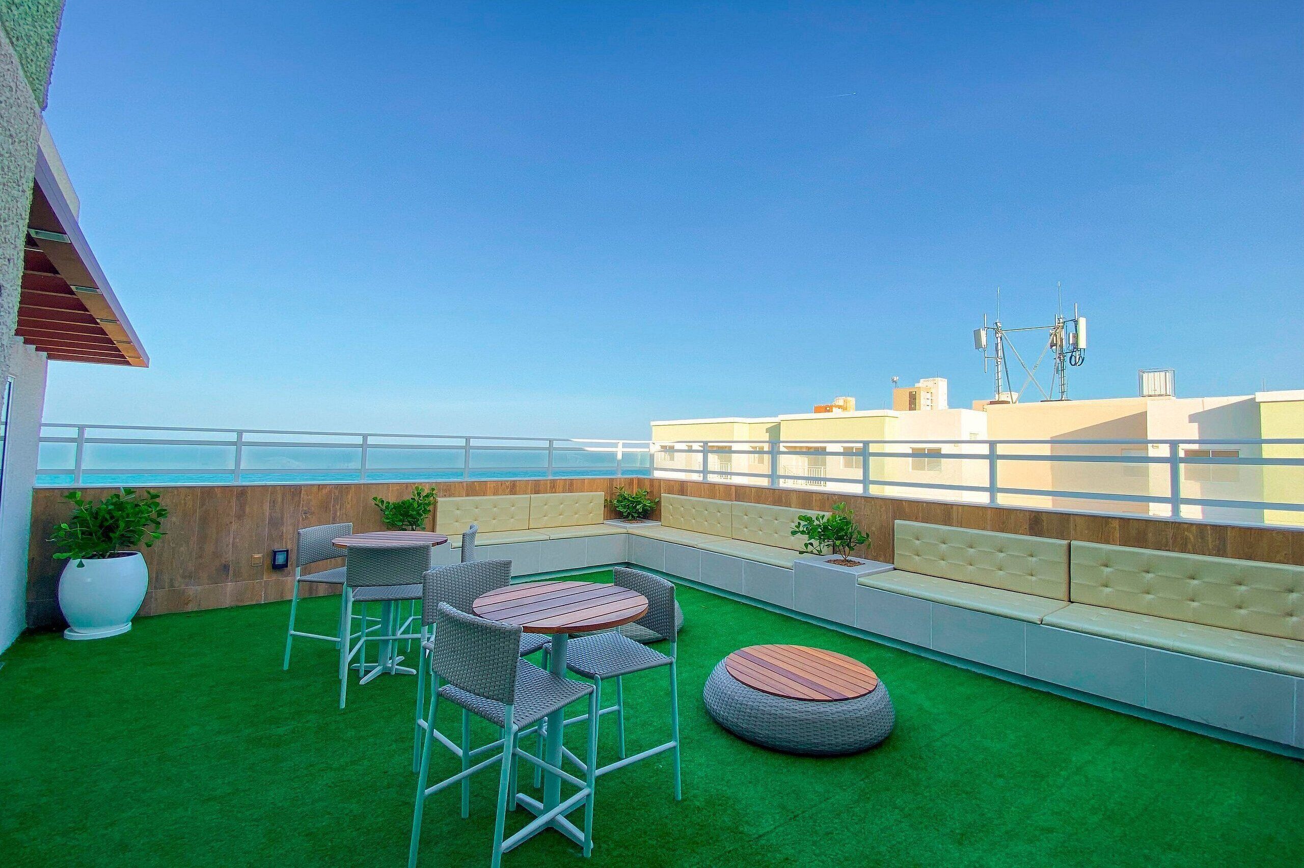 Terraço no telhado com grama sintética verde, áreas de estar e vista para o mar.