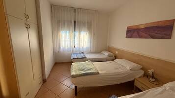 Quarto de hotel com duas camas de solteiro, um guarda-roupa, uma janela com cortinas e um quadro na parede.