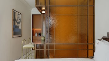 Quarto de hotel com cama, escrivaninha, cadeira, pintura e um separador decorativo.