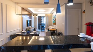 Cozinha moderna com ilha de mármore, luminárias pendentes e área de jantar com sofá e mesa.
